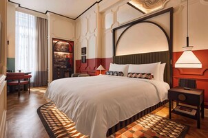 Quarto de hotel com uma cama grande, uma escrivaninha, uma cadeira, uma televisão e uma estante de livros.