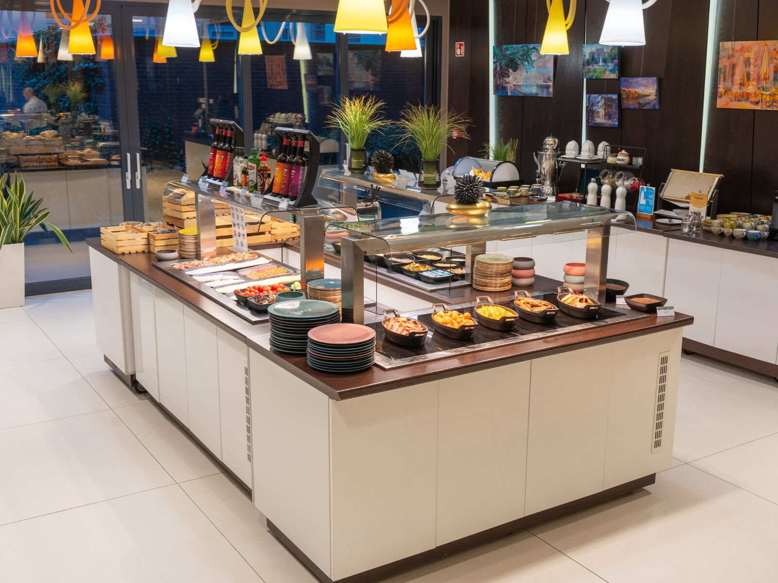Disposição de buffet com diversos alimentos, uma vitrine de vidro e iluminação pendente.