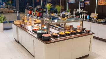 Disposição de buffet com diversos alimentos, uma vitrine de vidro e iluminação pendente.