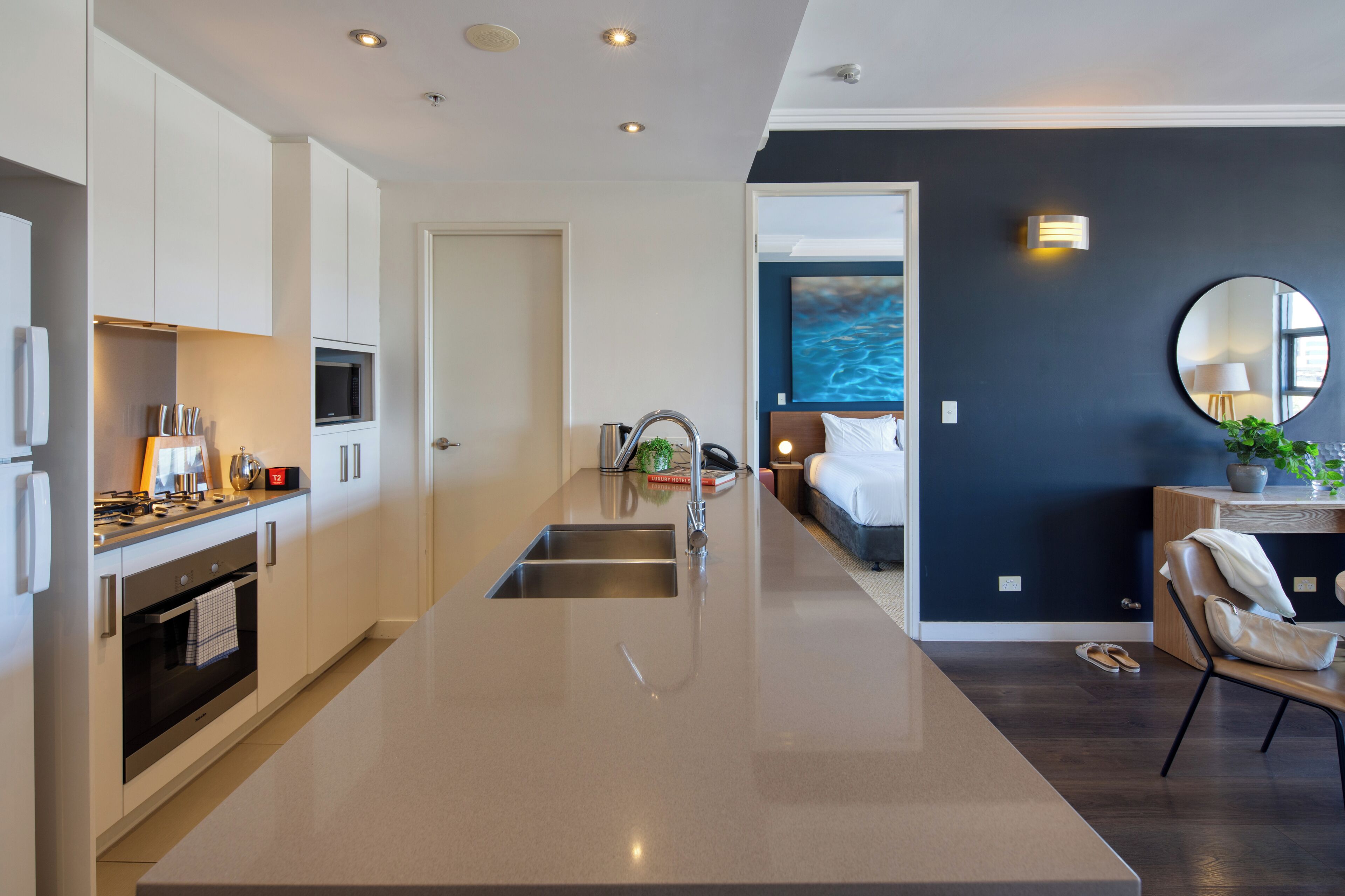 Cozinha moderna com ilha central, eletrodomésticos de aço inoxidável e vista para um quarto com uma janela grande.