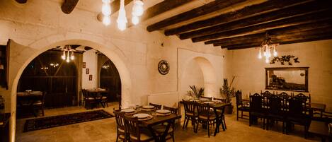 Uma área de jantar com mesas e cadeiras de madeira, um candelabro e teto rústico.