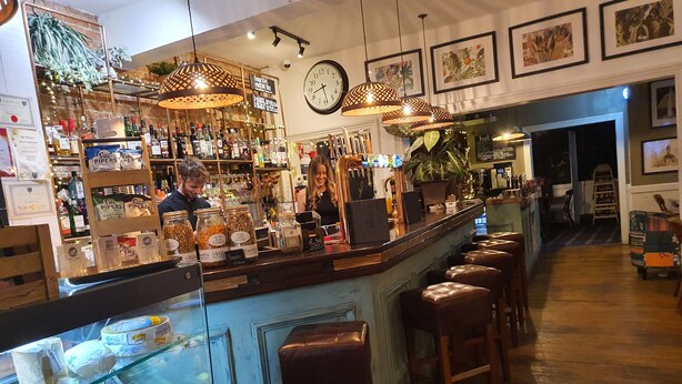 Uma área de bar com bancos, um relógio e diversos frascos e potes nas prateleiras.