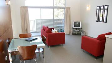 Uma sala de estar moderna com uma mesa de vidro, sofás vermelhos e uma televisão.