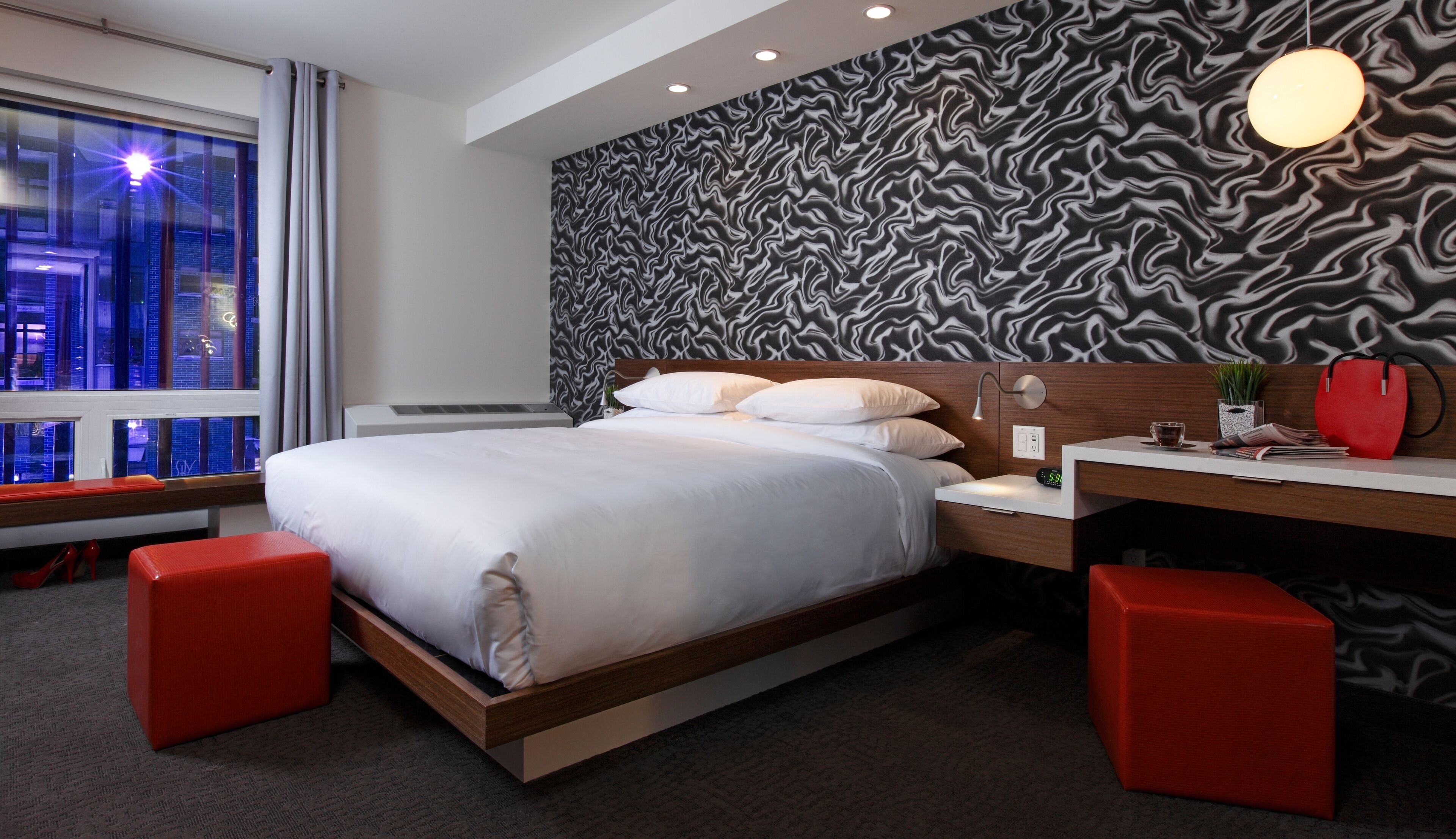 Quarto de hotel moderno com cama, mesa de cabeceira e vista para a cidade à noite.
