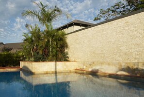 Uma piscina com muro revestido e palmeiras.