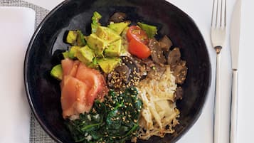 Uma tigela preta com diversos alimentos como abacate, salmão e vegetais, com um garfo e uma faca ao lado.