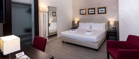 Quarto de hotel com cama, mesas de cabeceira, escrivaninha com abajur, cadeira e espelho.