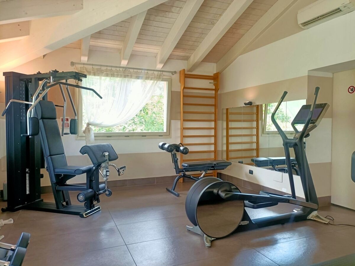 Uma academia com equipamentos de ginástica, esteira e uma janela com cortinas.