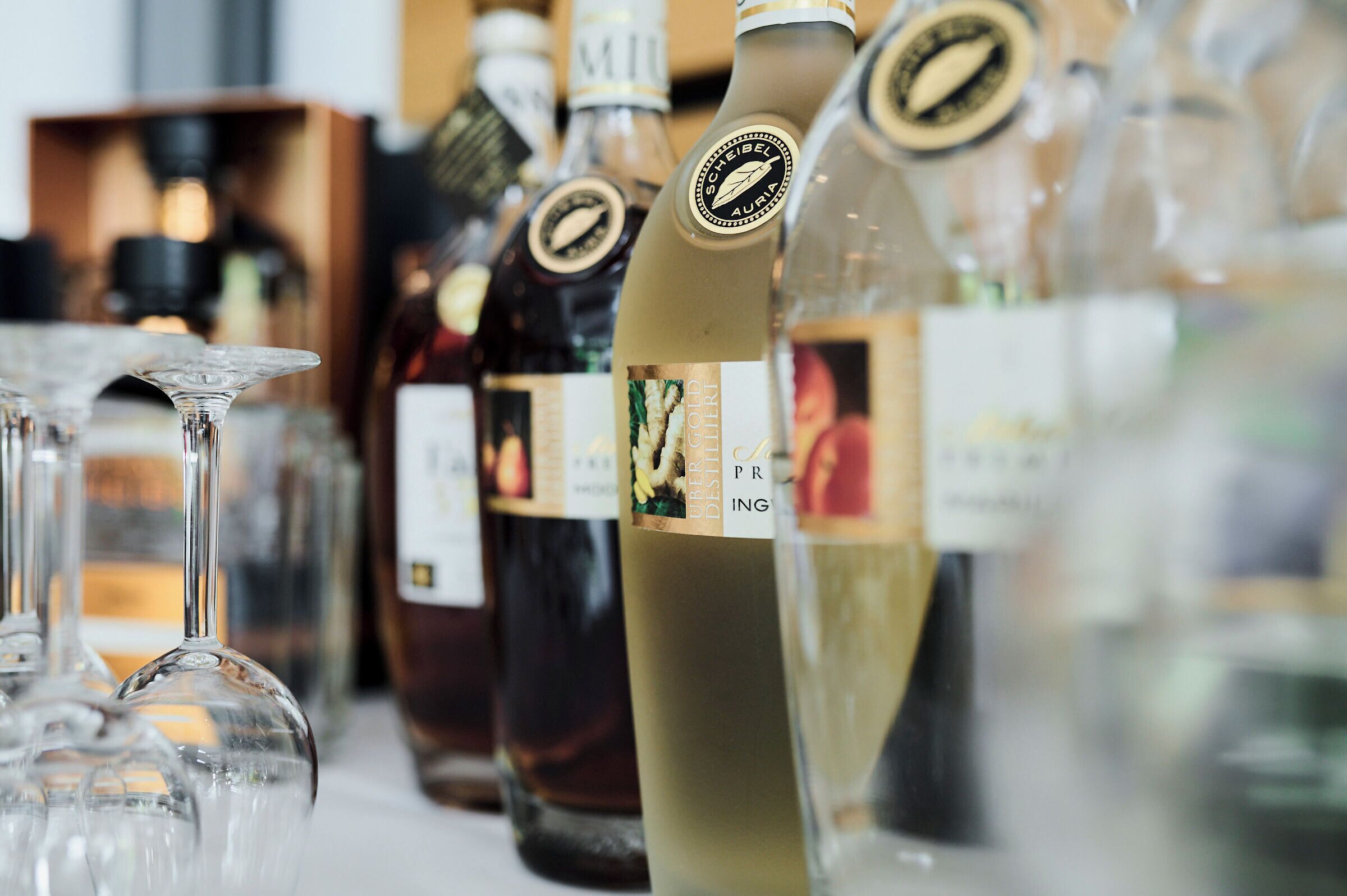Várias garrafas de vinho com etiquetas e um copo em primeiro plano.