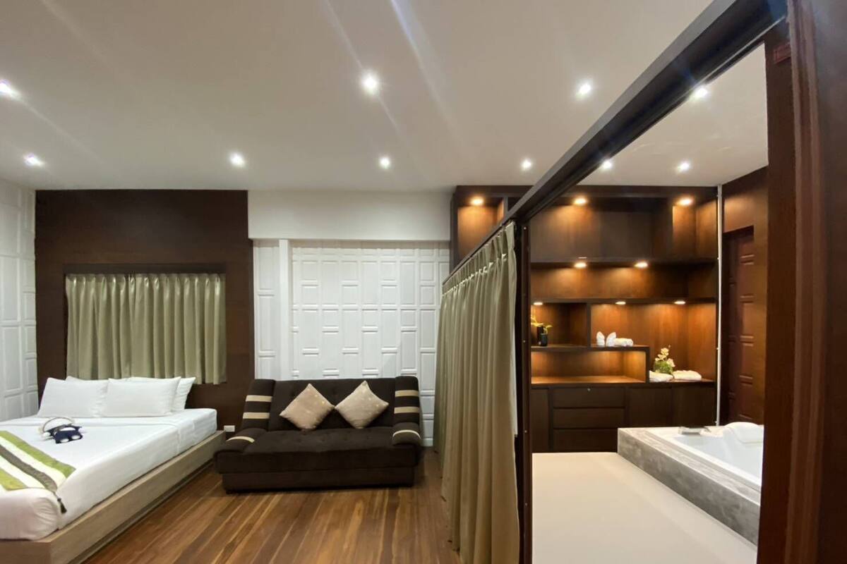 Quarto de hotel com cama, sofá, mesinha e espaço para o banheiro.