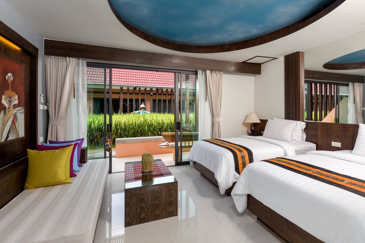 Quarto de hotel moderno com duas camas, porta de vidro que dá para uma varanda e um espelho grande.