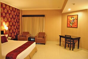 Quarto de hotel com uma cama grande, duas poltronas, uma mesa de jantar e um quadro na parede.