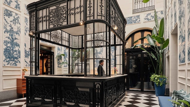 Piso quadriculado em preto e branco, grades de metal preto ornamentadas e paredes com padrão azul e branco.