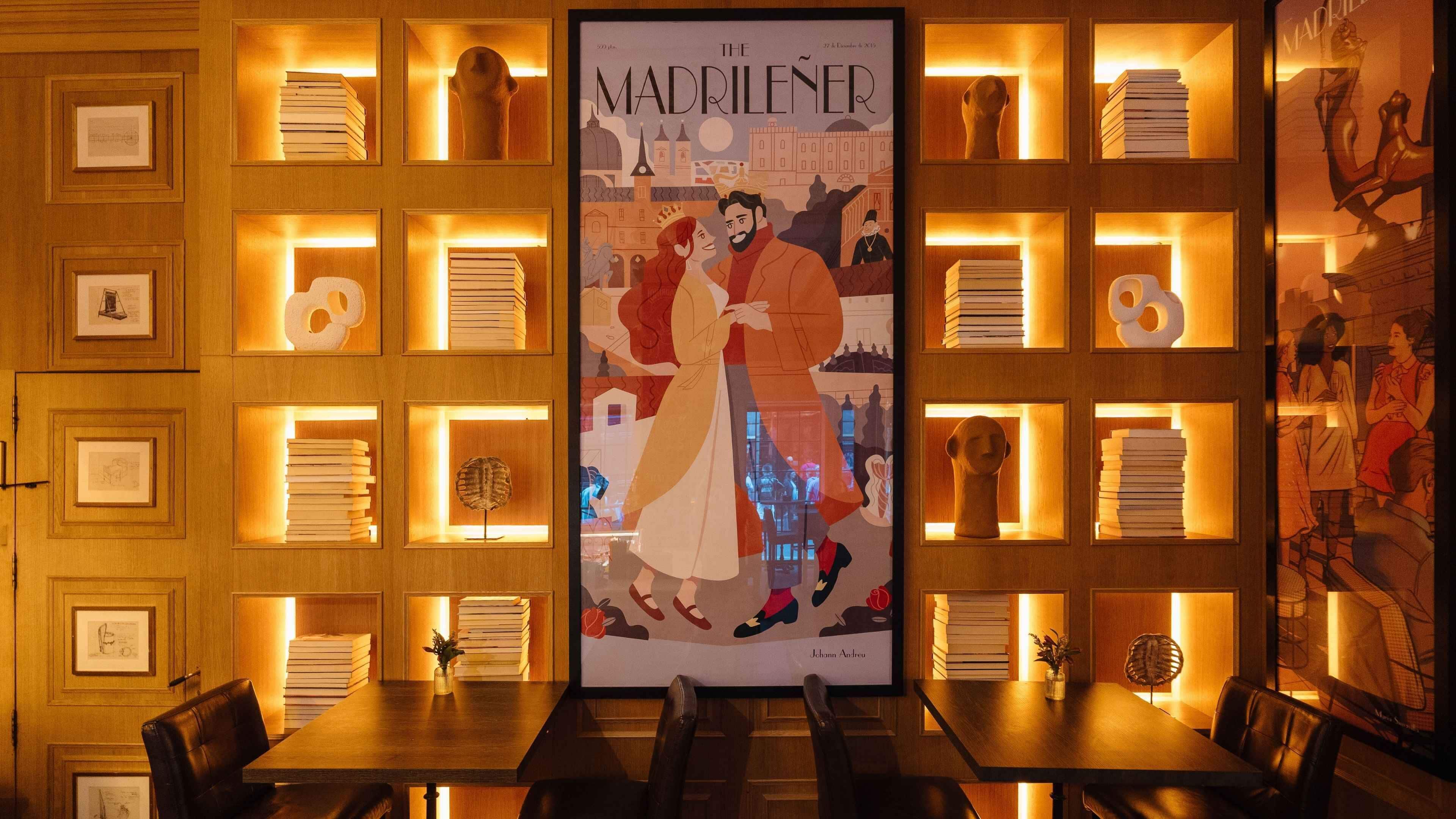 Um restaurante com um grande cartaz de 'The Madrileners' e prateleiras com livros e esculturas.