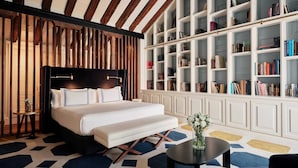 Quarto com uma cama grande, uma estante de livros e uma mesa pequena com um vaso de flores.