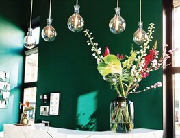 Uma área de recepção com uma parede verde, um balcão de recepção branco e um vaso de flores.