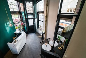 Um interior moderno com uma mesa de recepção, duas mesas redondas e prateleiras com objetos decorativos.