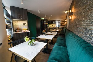 Um restaurante moderno com parede verde, mesas de mármore e um sofá verde-água.