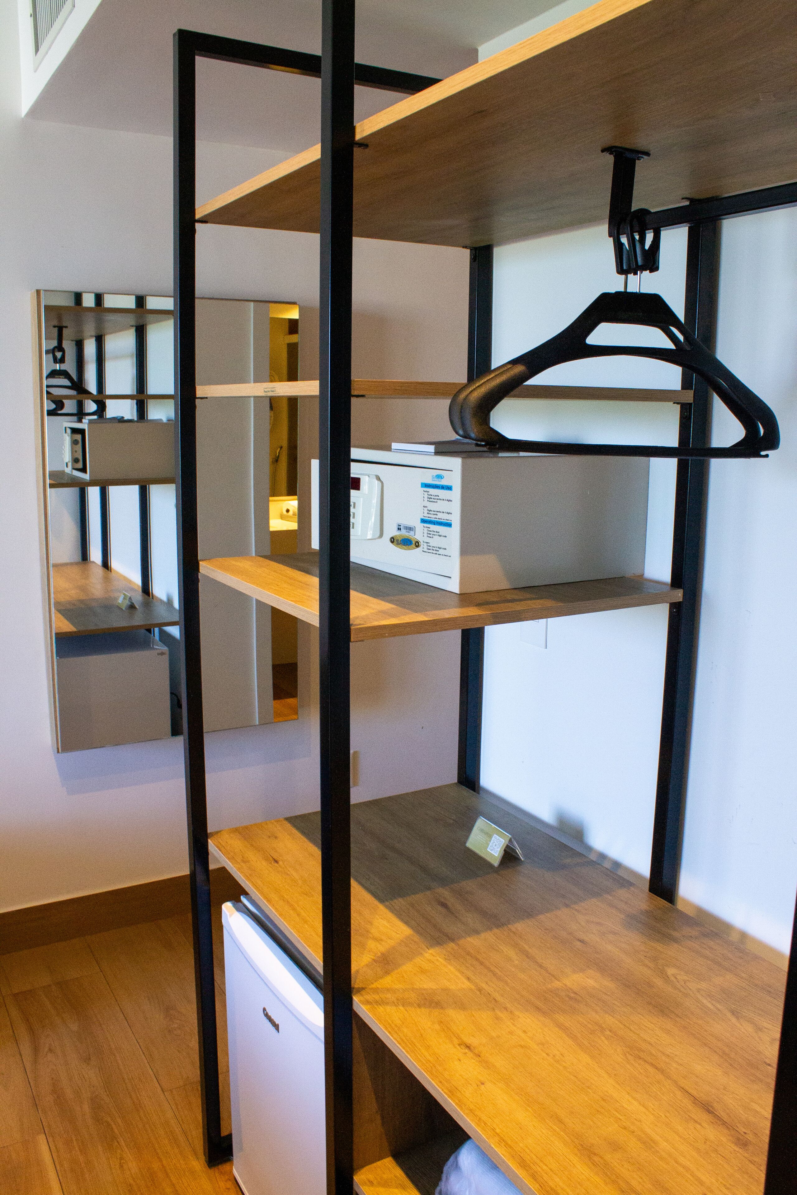 Quarto compacto com prateleiras de madeira embutidas, um eletrodoméstico pequeno branco e um espelho.