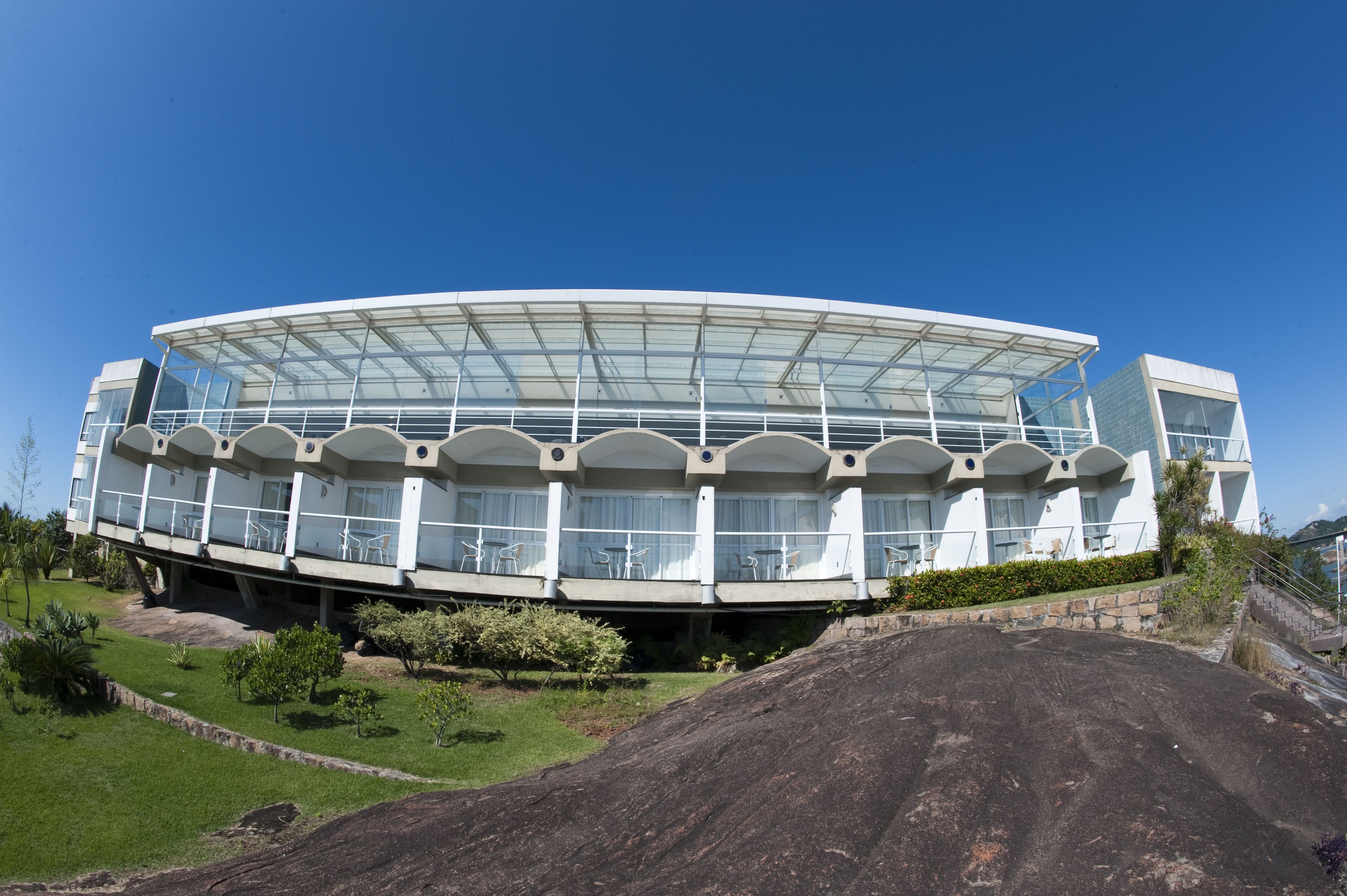Um edifício moderno com fachada curva, grandes janelas e uma área externa coberta com assentos.