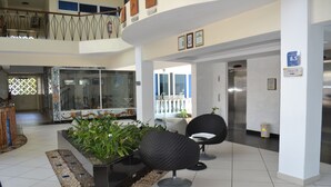 Um hall amplo com design moderno, com área de estar com uma cadeira preta, divisória de vidro e arranjo de plantas.