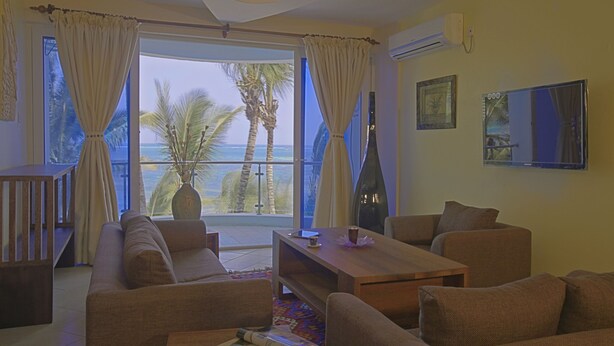 Sala de estar com sofá, mesa de centro e vista para o oceano através de grandes janelas.