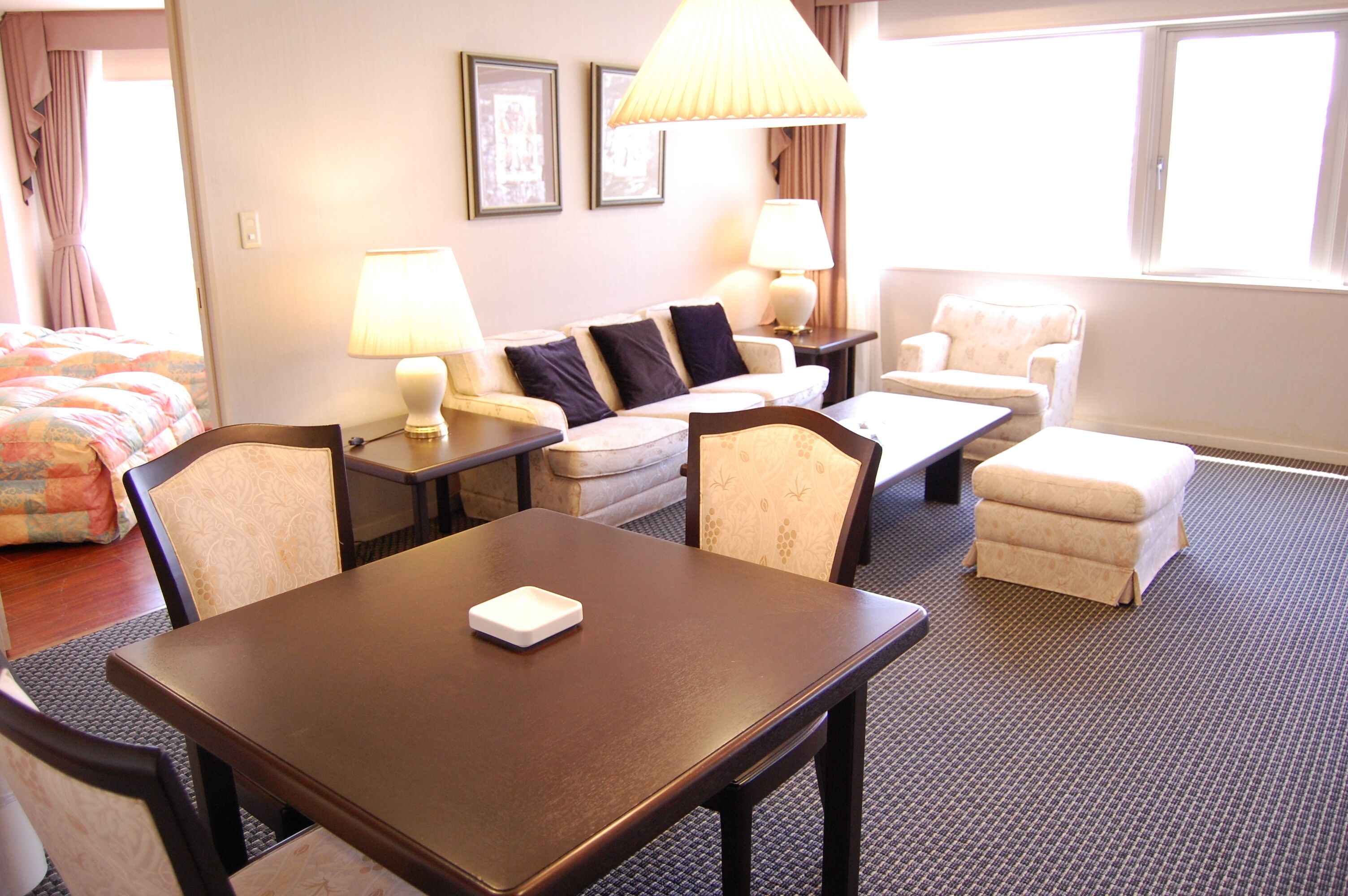 Quarto de hotel com uma cama, um sofá, uma mesa de jantar e duas luminárias.