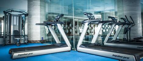 Uma academia com duas esteiras de corrida modelo 'impulse pro', um aparelho de musculação e um banco.