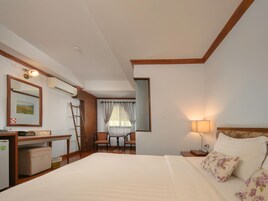Quarto de hotel com cama, escrivaninha, cadeira, luminária e janela com cortinas.