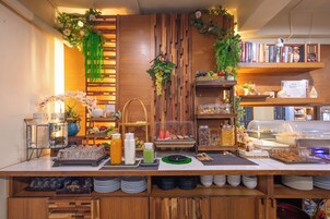 Disposição de buffet com diversos alimentos, um espaço para café e uma seleção de livros em estantes.