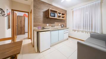 Uma cozinha compacta com micro-ondas, pia e armários. Há uma mesa de jantar e um sofá na sala de estar.