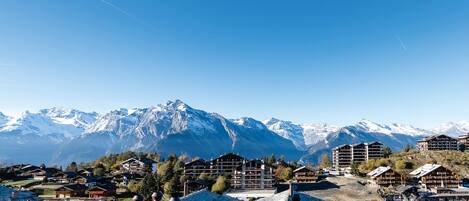 Um resort de montanha com edifícios em estilo chalé, picos nevados ao fundo e um céu azul límpido.