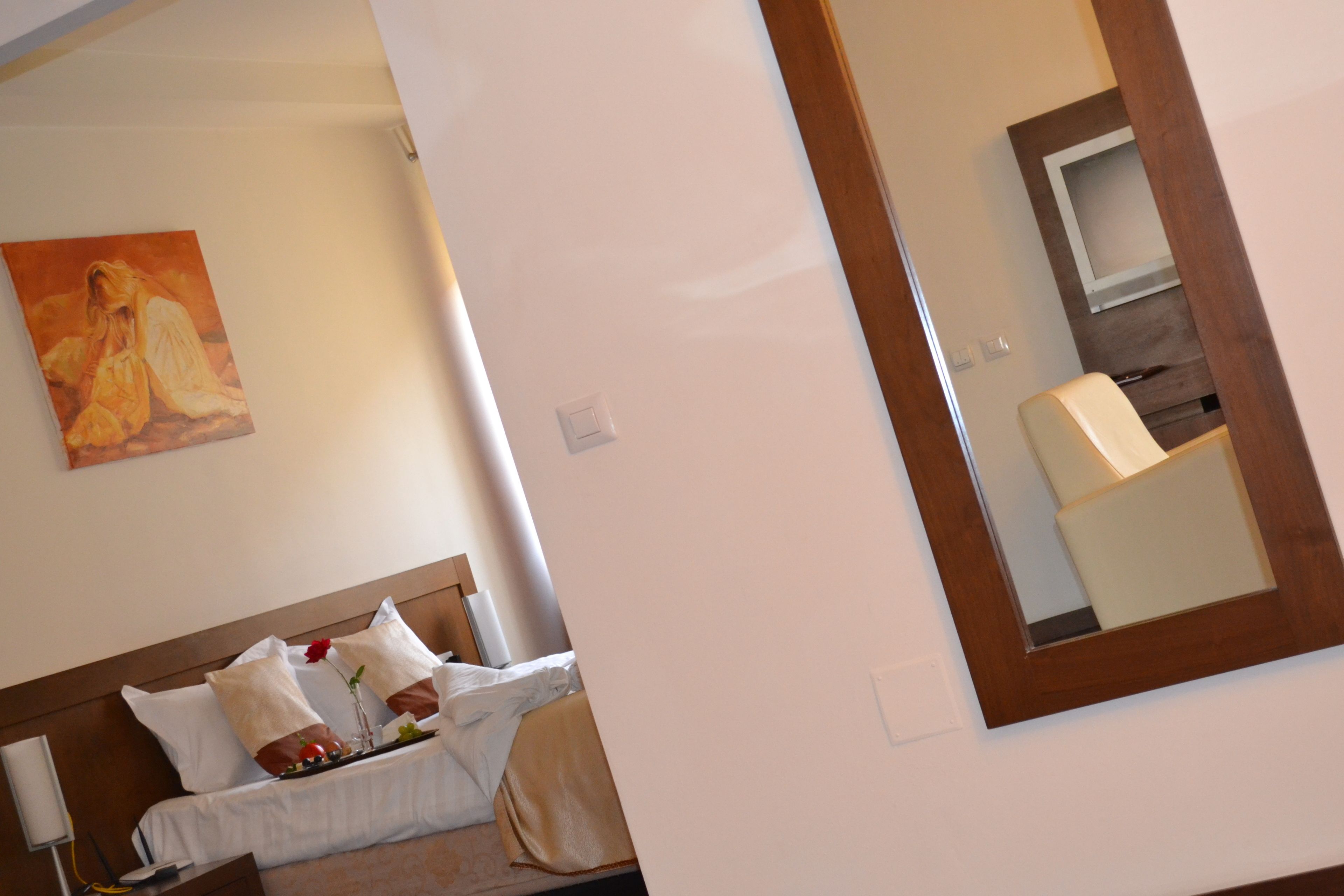 Quarto de hotel com uma cama, mesa de cabeceira, espelho e um quadro na parede.