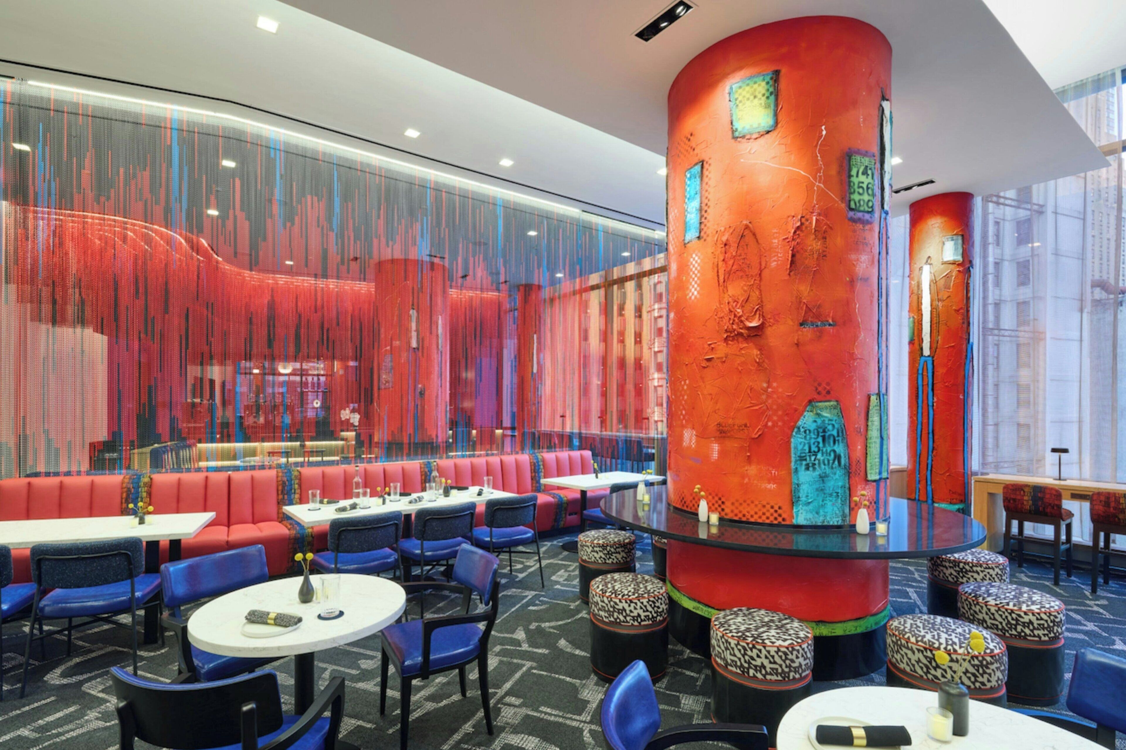 Um restaurante moderno com mesas redondas, cadeiras azuis e sofás vermelhos.