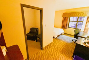 Quarto de hotel com uma cama, escrivaninha, cadeira e janela com cortinas.