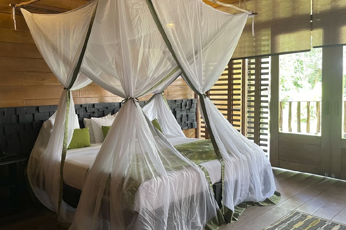Quarto com uma cama de dossel, mesa de cabeceira e vista para o verde lá fora.