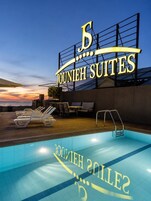 Placa de hotel com 'Jounieh Suites' e área de piscina com espreguiçadeiras e piscina.