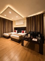 Quarto de hotel com duas camas, um sofá, uma mesa de centro e uma escrivaninha com telefone e menu.