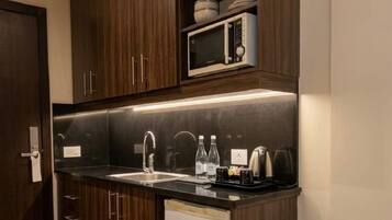 Cozinha compacta com armários de madeira escura, micro-ondas, pia e lava-louça.