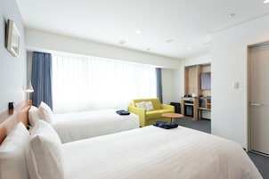 Quarto de hotel com duas camas, um sofá, uma mesinha e uma cozinha compacta.