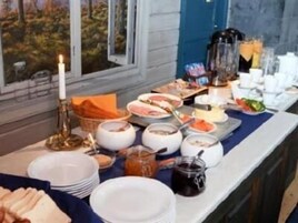 Disposição de buffet com diversos alimentos, incluindo frutas, queijos e acompanhamentos, sobre uma mesa com vista para árvores.