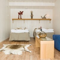Quarto com duas camas, mesa de centro de madeira, sofá azul, tapete de pele e prateleiras fixadas na parede com objetos decorativos.