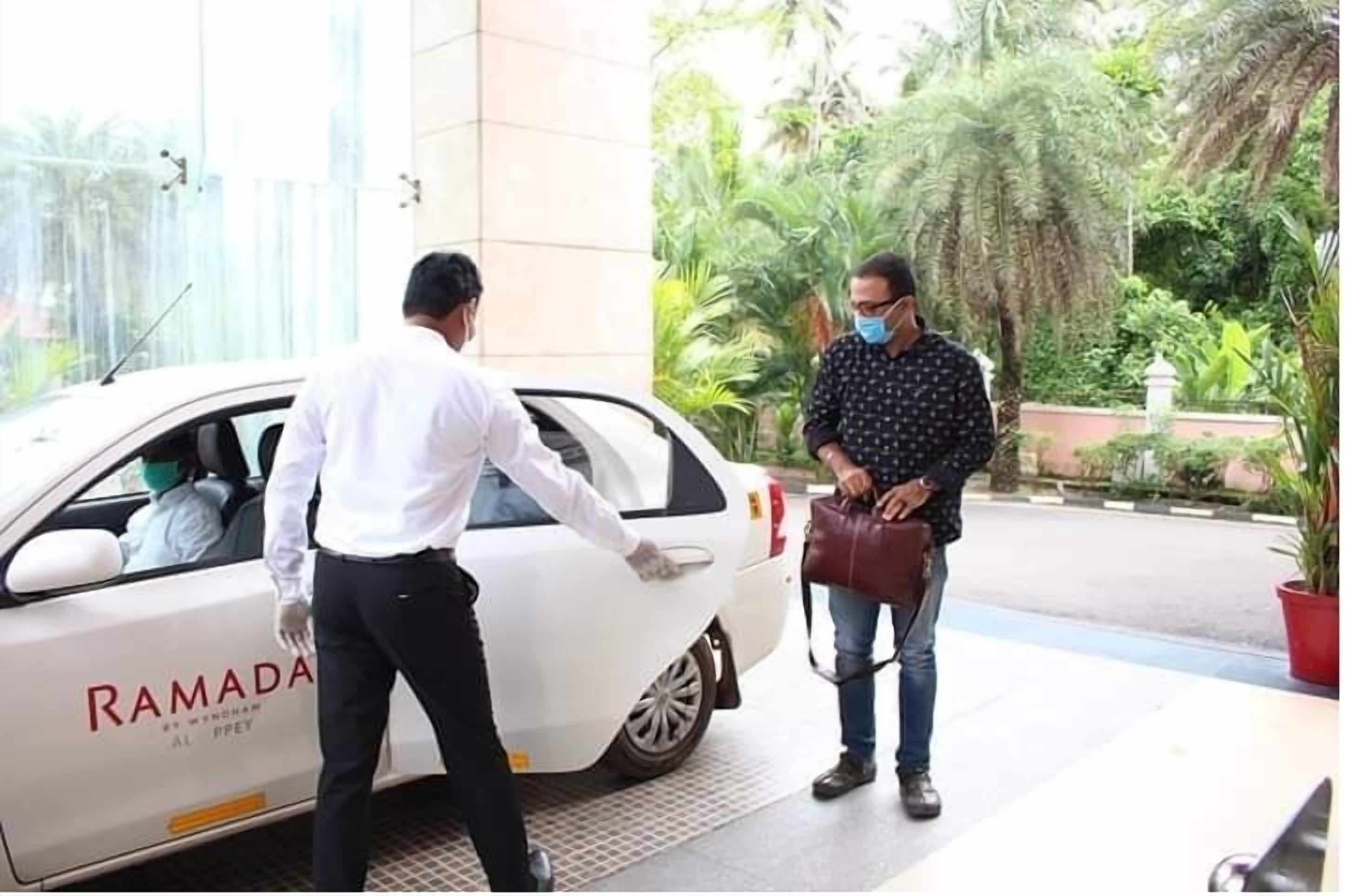 Um carro branco com a inscrição 'RAMADA', estacionado em frente a um edifício com entrada em azulejos.