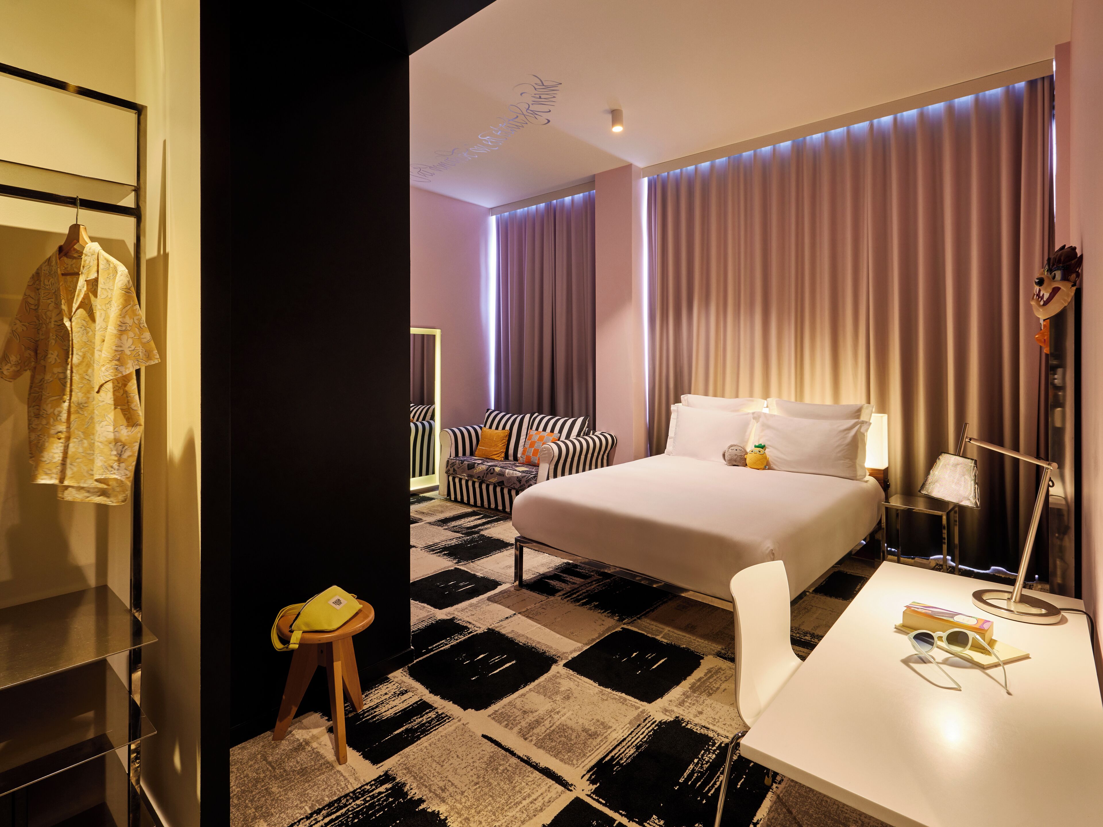 Quarto de hotel com cama, escrivaninha, cadeira, sofá e guarda-roupa.