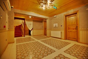 Um hall de hotel com piso estampado, escada, portas de madeira e um candelabro.