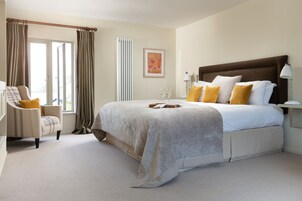 Quarto com cama grande, uma cadeira, janela com cortinas e radiador.
