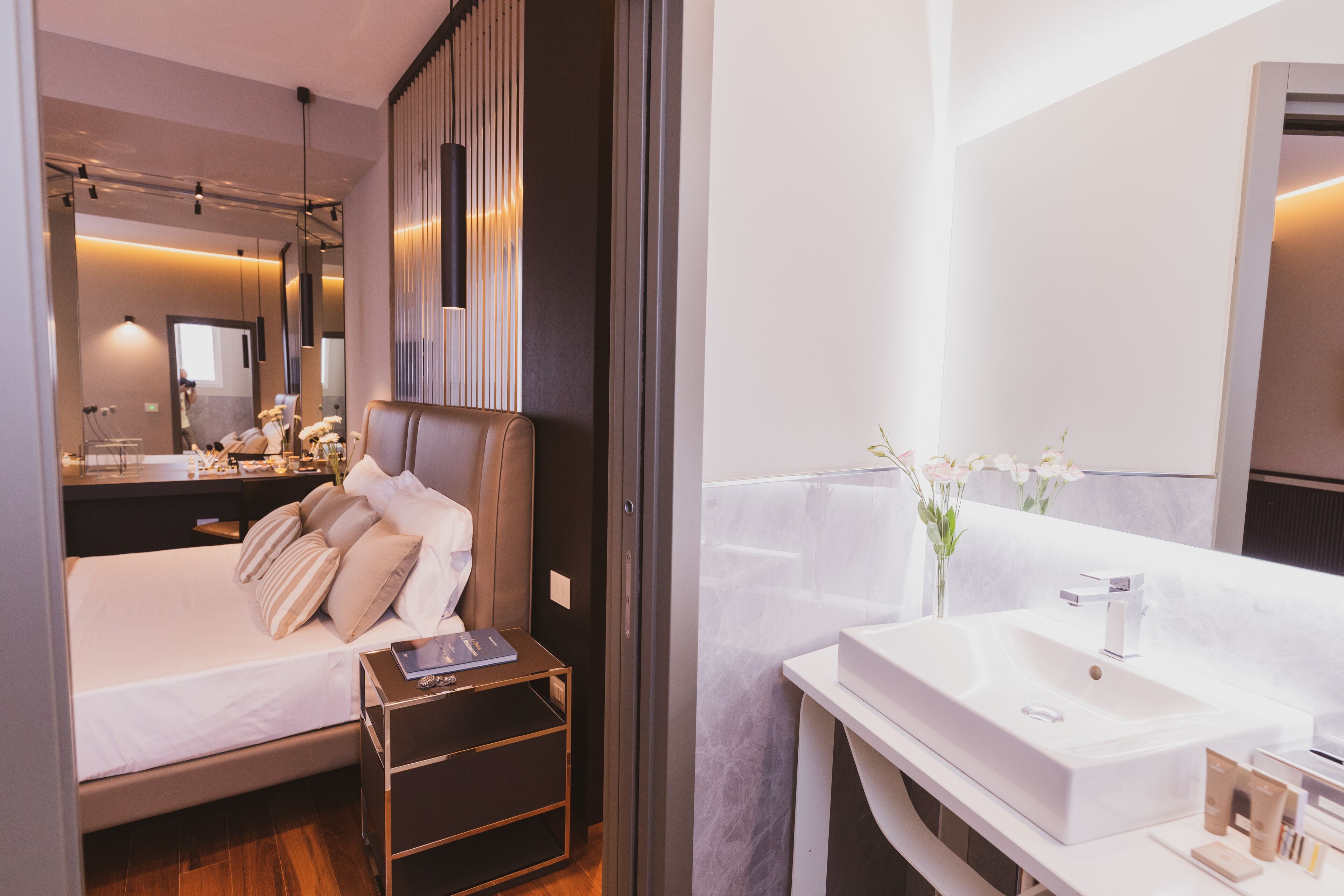 Quarto de hotel moderno com cama, mesa de cabeceira e um espelho grande sobre a pia.