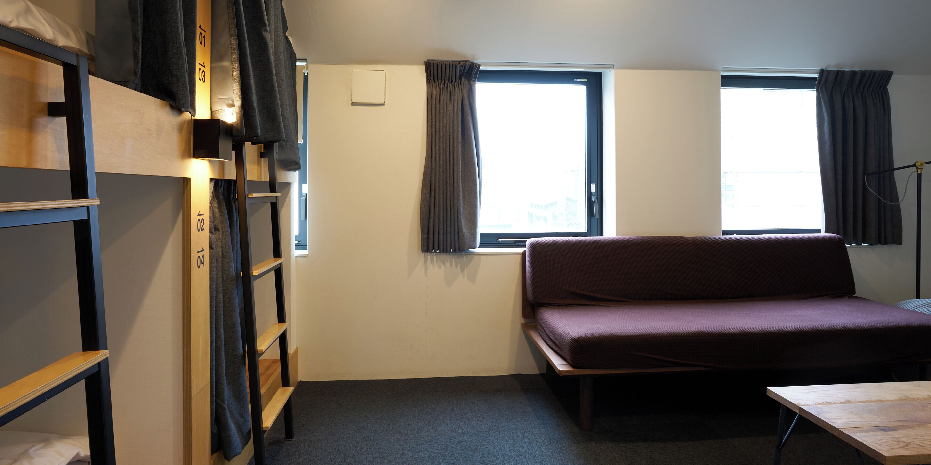 Quarto com beliches, sofá, mesa e duas janelas com cortinas.