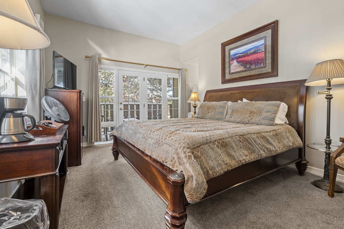 Quarto com uma cama grande, uma escrivaninha com luminária, uma cadeira e vista para o exterior através de uma porta de vidro.