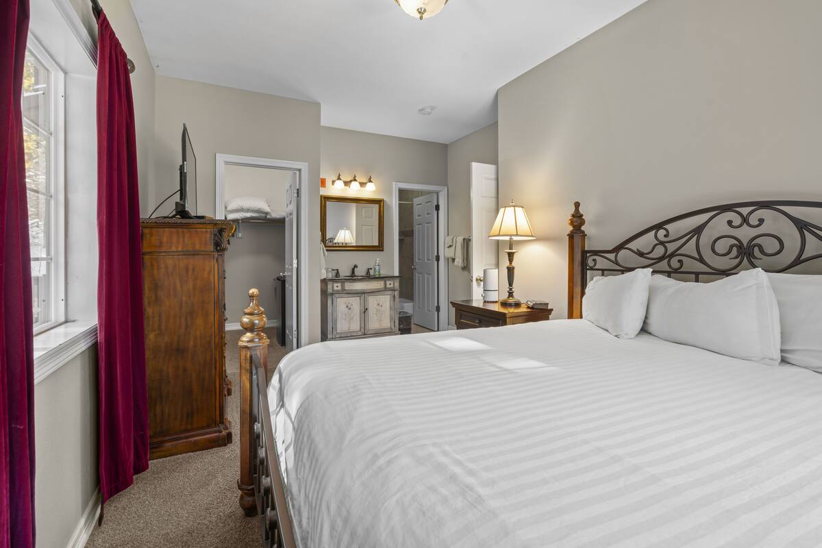 Quarto com uma cama grande, penteadeira de madeira, toucador com espelho e janela com cortinas vermelhas.